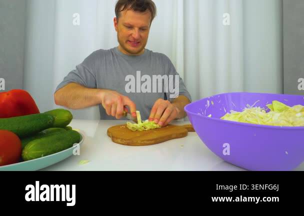 A man prepares a vegetable salad, chopped white cabbage in a salad ...