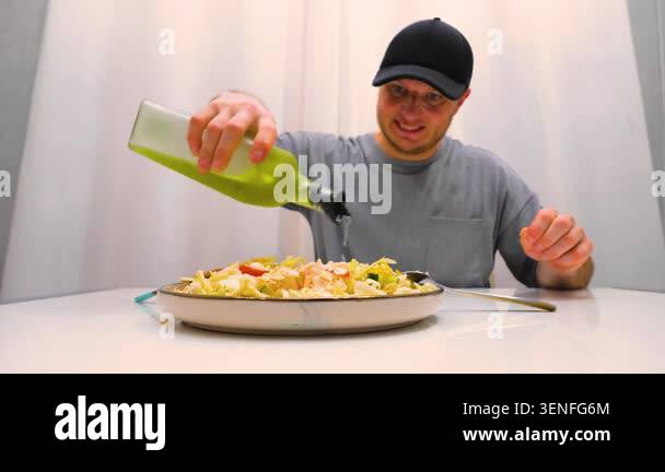 Drizzle olive oil over fresh salad. A man prepares a salad of ...