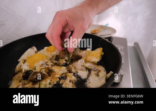 Cooking an omelet, a young man frying scrambled eggs in a frying pan ...