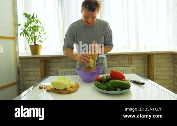A man is preparing a vegetable salad, cutting white cabbage in the ...