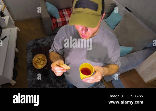 Dip cookies into a cup of tea and eat. A young man has breakfast with ...