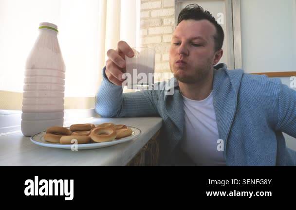 A man has breakfast with yogurt and cookies. A young guy drinks yogurt ...