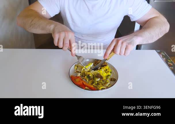 A man is having dinner at the table in the kitchen, eating an omelet ...