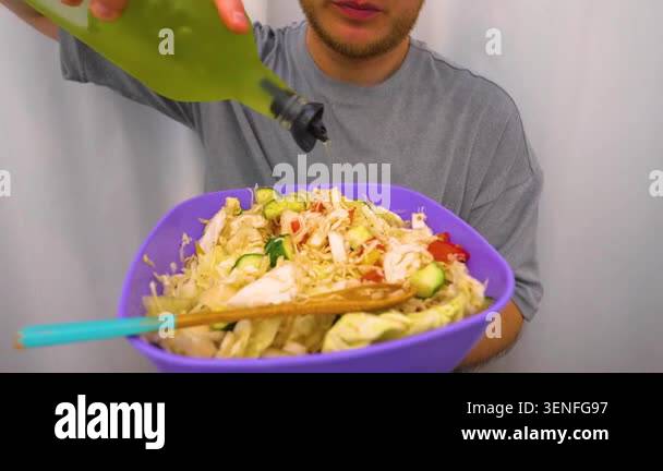 Drizzle olive oil over the salad. A man prepares a salad of vegetables ...