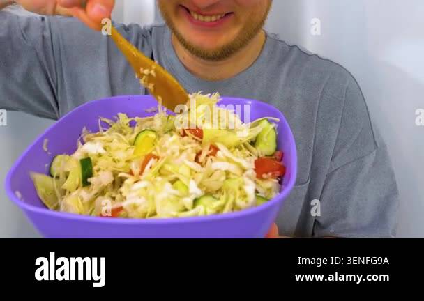Stir the fresh salad with a wooden spoon. A man prepares a salad of ...