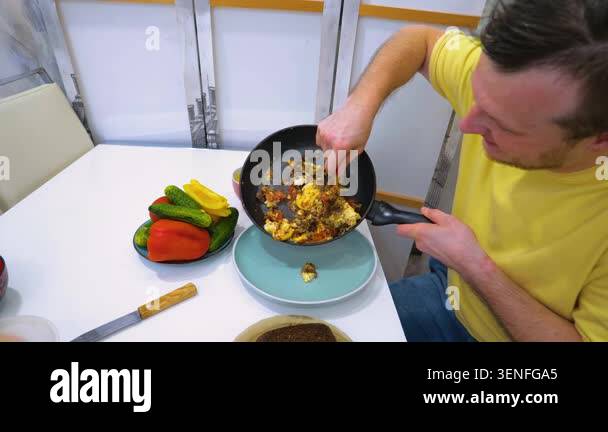 A man is preparing dinner at home, an omelette with tomatoes fried in a ...