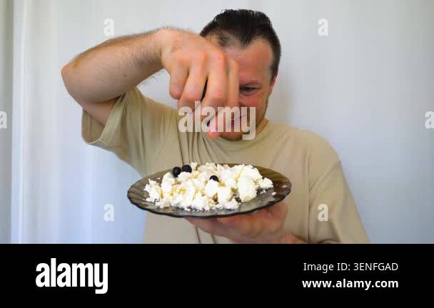 A man sprinkles blue berries into cottage cheese, healthy food, cooking ...
