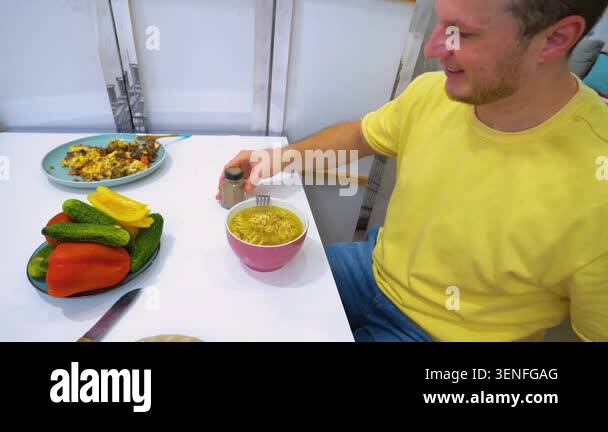 A young man is having dinner at the kitchen table, food on a plate is ...
