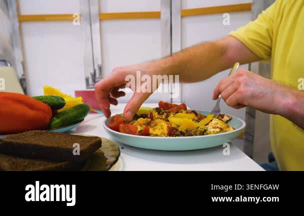 A man is preparing dinner at home, an omelette with tomatoes fried in a ...