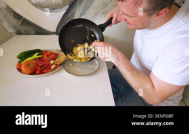 Cooking dinner from an omelet, a young man pours scrambled eggs into a ...
