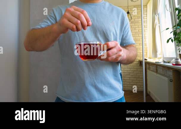 Place the tea bag into the cup. A man with hot brewed tea in a ...