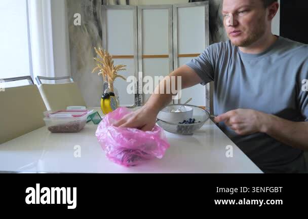 A man pours blue berries into a sieve while preparing food in the ...