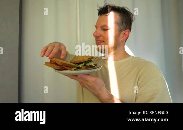 A young man eats a delicious sandwich from a plate. In slow motion. A ...