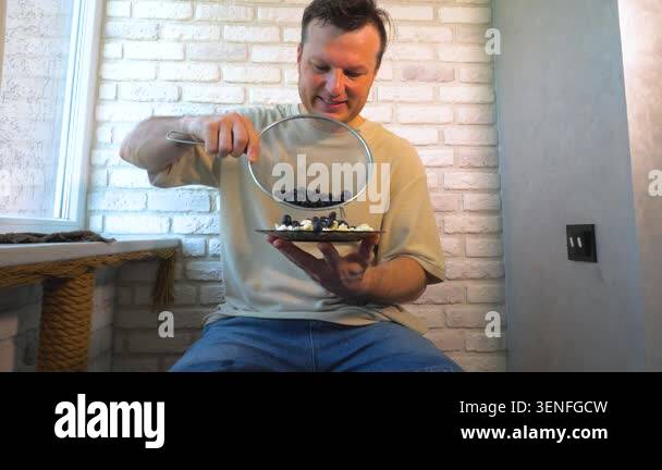 A man sprinkles blue berries into cottage cheese, healthy food, cooking ...