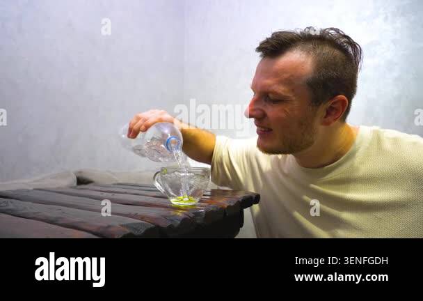 A man pours drinking water from a plastic bottle into a transparent cup ...
