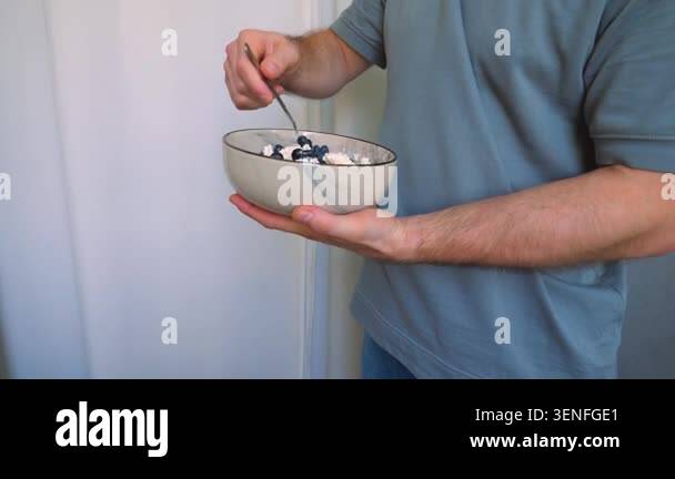 Cottage cheese with blue berries in a plate. A young man prepares food ...