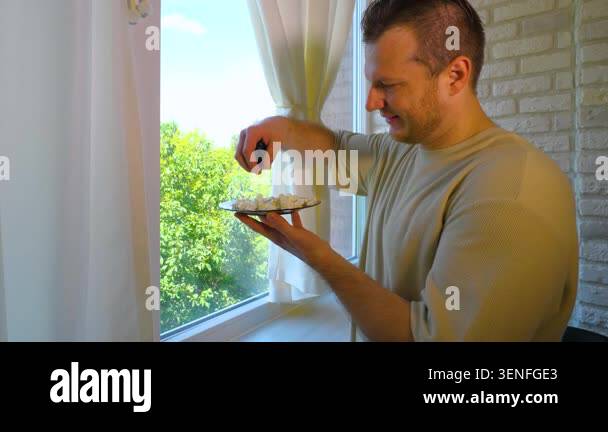 A man sprinkles blue berries into cottage cheese in the kitchen ...
