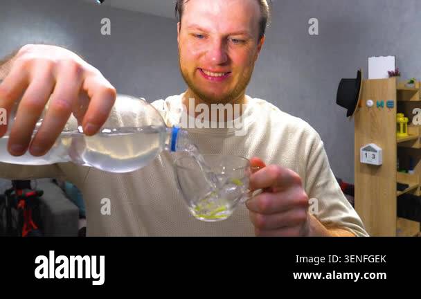 A man pours drinking water from a plastic bottle into a transparent cup ...