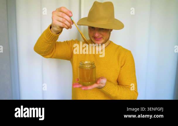Scoop out honey with a wooden spoon. A young man holds a jar of bee ...