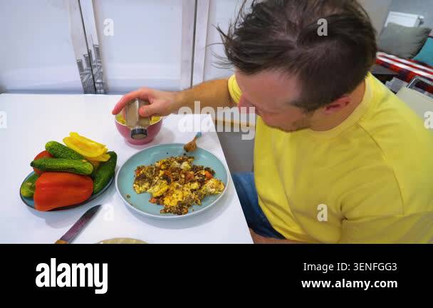 A young man is having dinner at the kitchen table, food is on an omelet ...
