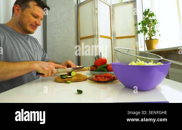 A man cuts a cucumber on a cutting board, cutting vegetable salad in ...