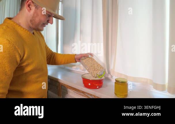 Cooking oatmeal at home, a young man pours oat grains into a pan. Slow ...