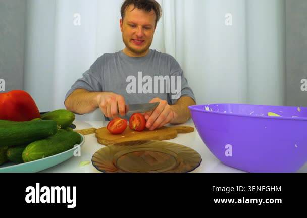 A man cuts a tomato on a cutting board, cutting vegetable salad in the ...