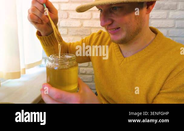 Scoop out honey with a wooden spoon. A young man holds a jar of bee ...