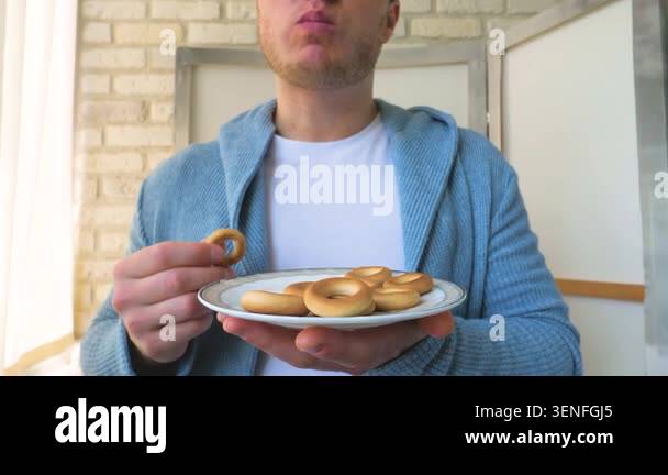 A young guy eats pastries in the form of rings. Eating bagel cookies in ...