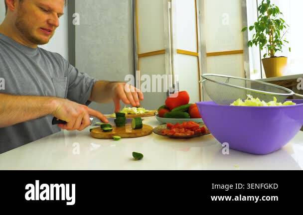 A man cuts a cucumber on a cutting board, cutting vegetable salad in ...