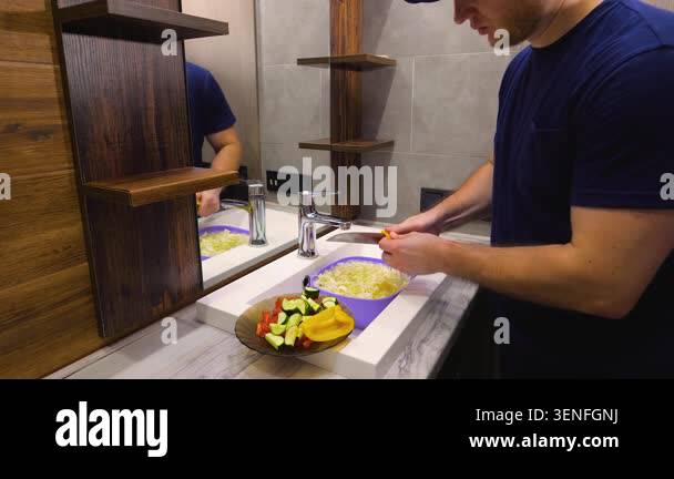 A man washes greens and chopped cabbage under the water tap. Prepare ...
