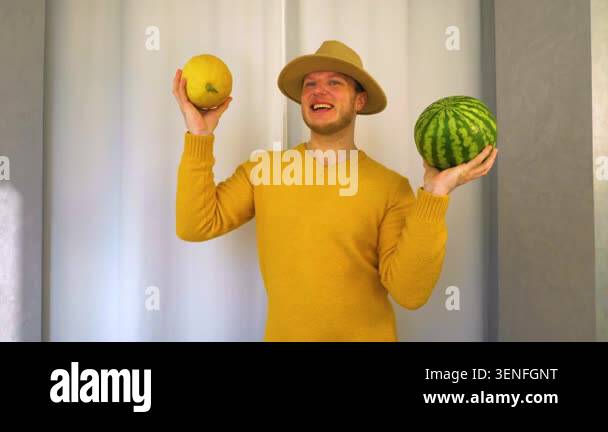 A man in bright clothes dances with a fruit melon and watermelon in his ...