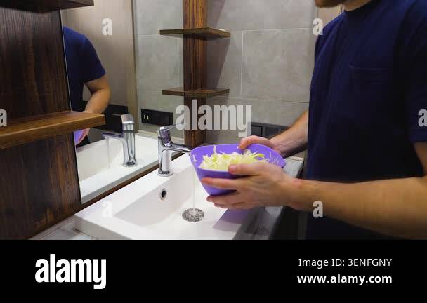 A man washes greens and chopped cabbage under the water tap. Wash the ...