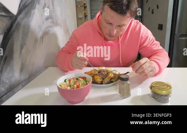 A man is having dinner, buckwheat with chicken wings, with salad in a ...