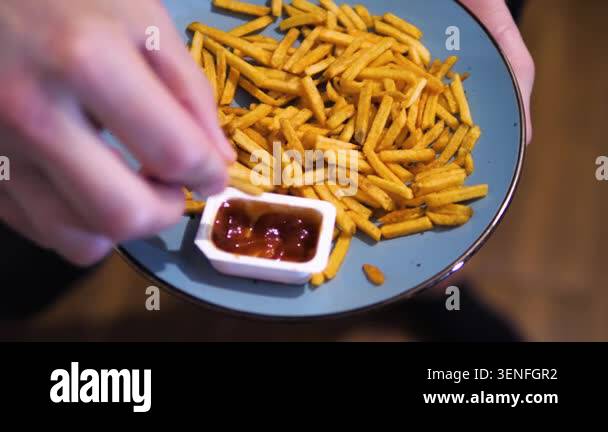 Man eats French fries with ketchup in an apartment. Male eat fast food ...
