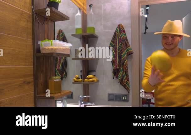 A young man washes a melon fruit under a water tap in an apartment. A ...