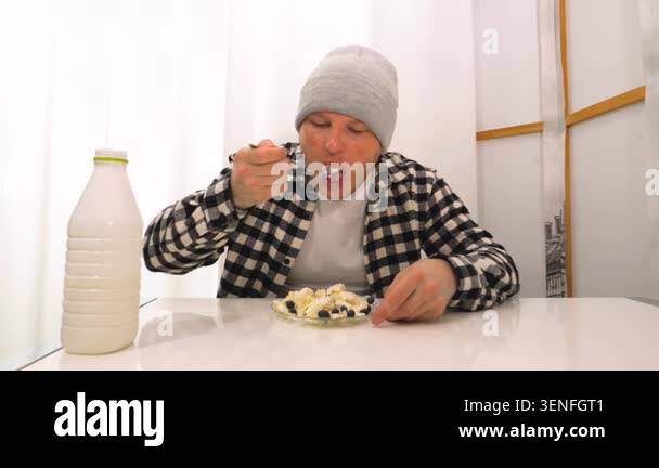 Pour yoghurt over cottage cheese and eat in the kitchen. A young man ...