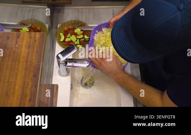 A man washes greens and chopped cabbage under the water tap. Prepare ...