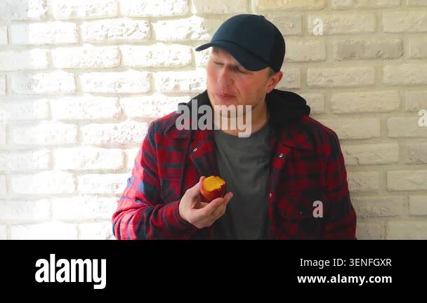 A young man eats a peach fruit against a background of a white brick ...
