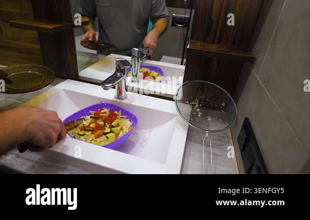 A man cuts greens, chopped cabbage. Prepare the salad, wash it under ...