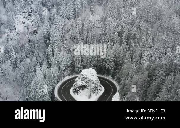 Cinematic drone shot pulling back from a winding mountain road curving ...