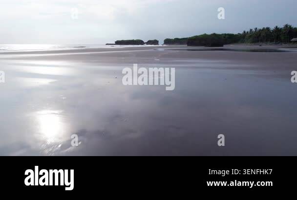 Drone footage shows a wide view of a Bali beach. The scene features wet ...