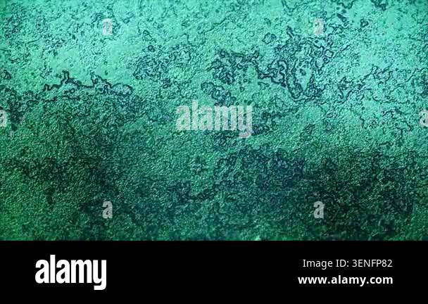 Slowly moving emerald green metallic fluid with a rough organic texture ...