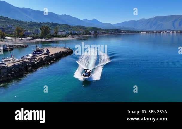 Front aerial view of a speedboat leaving a harbor with mountains ...