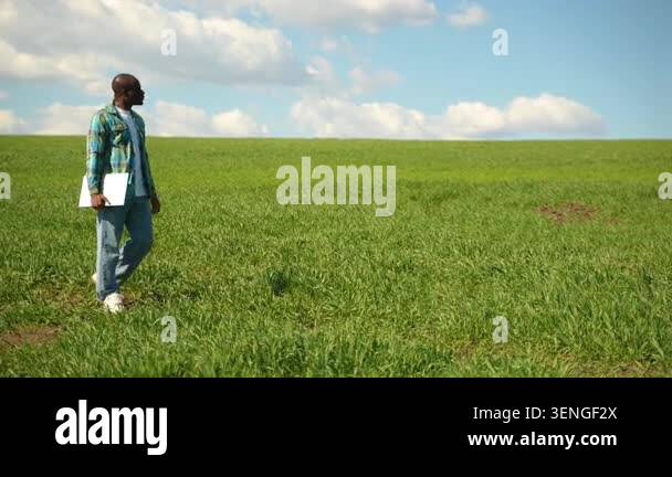 Modern farmer walking through a lush green field on a sunny day. The ...