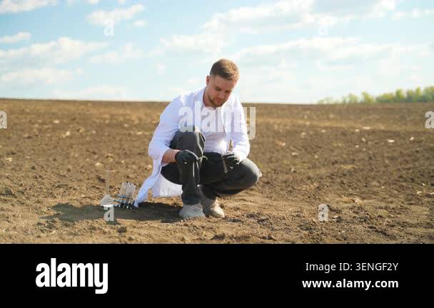 Agricultural scientist wearing a lab coat and gloves taking a soil ...