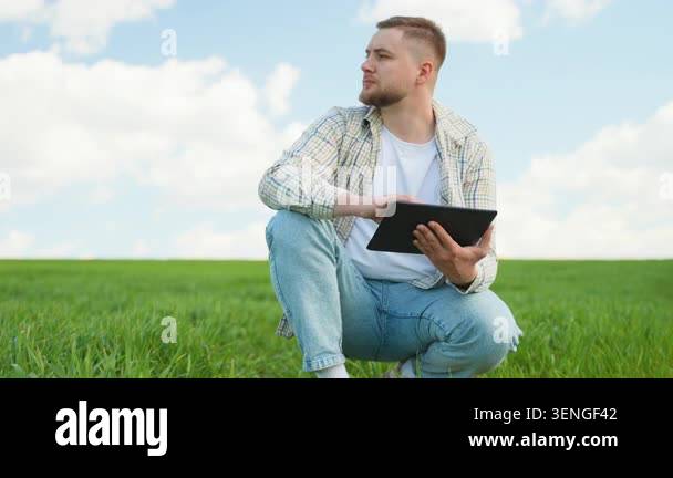 Young agronomist with a digital tablet squatting in a green wheat field ...
