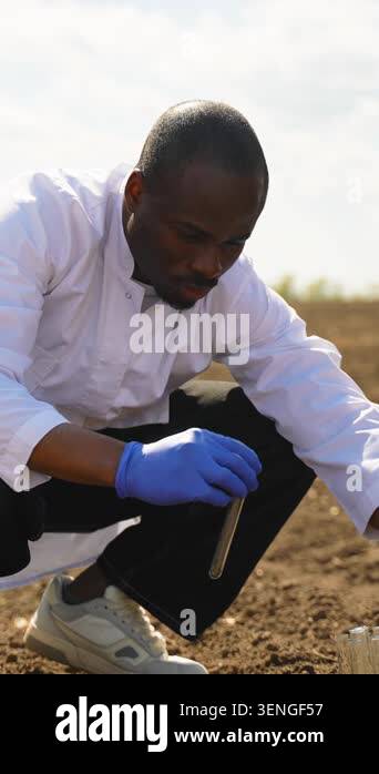 Male ecologist in a white lab coat and blue gloves collecting a soil ...