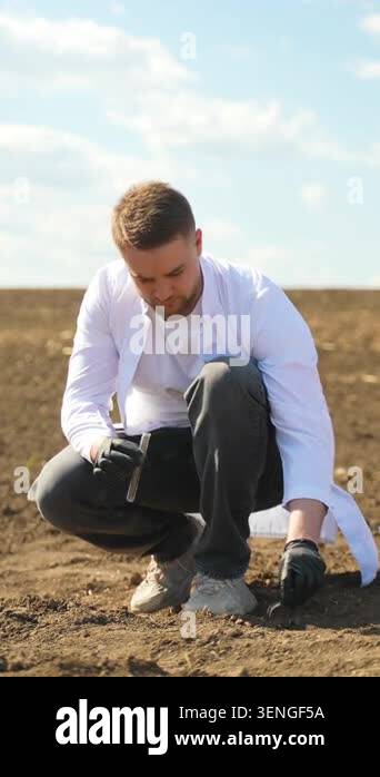 Male scientist in a white coat and gloves taking a soil sample from an ...
