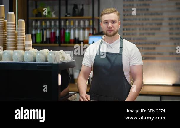Young male barista wearing an apron looking at the camera and smiling ...